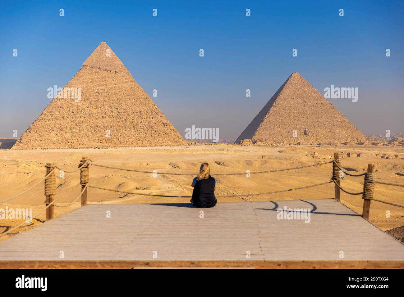 Blonde tourist sitting in front of the Gizah pyramids in Cairo, Egypt ...