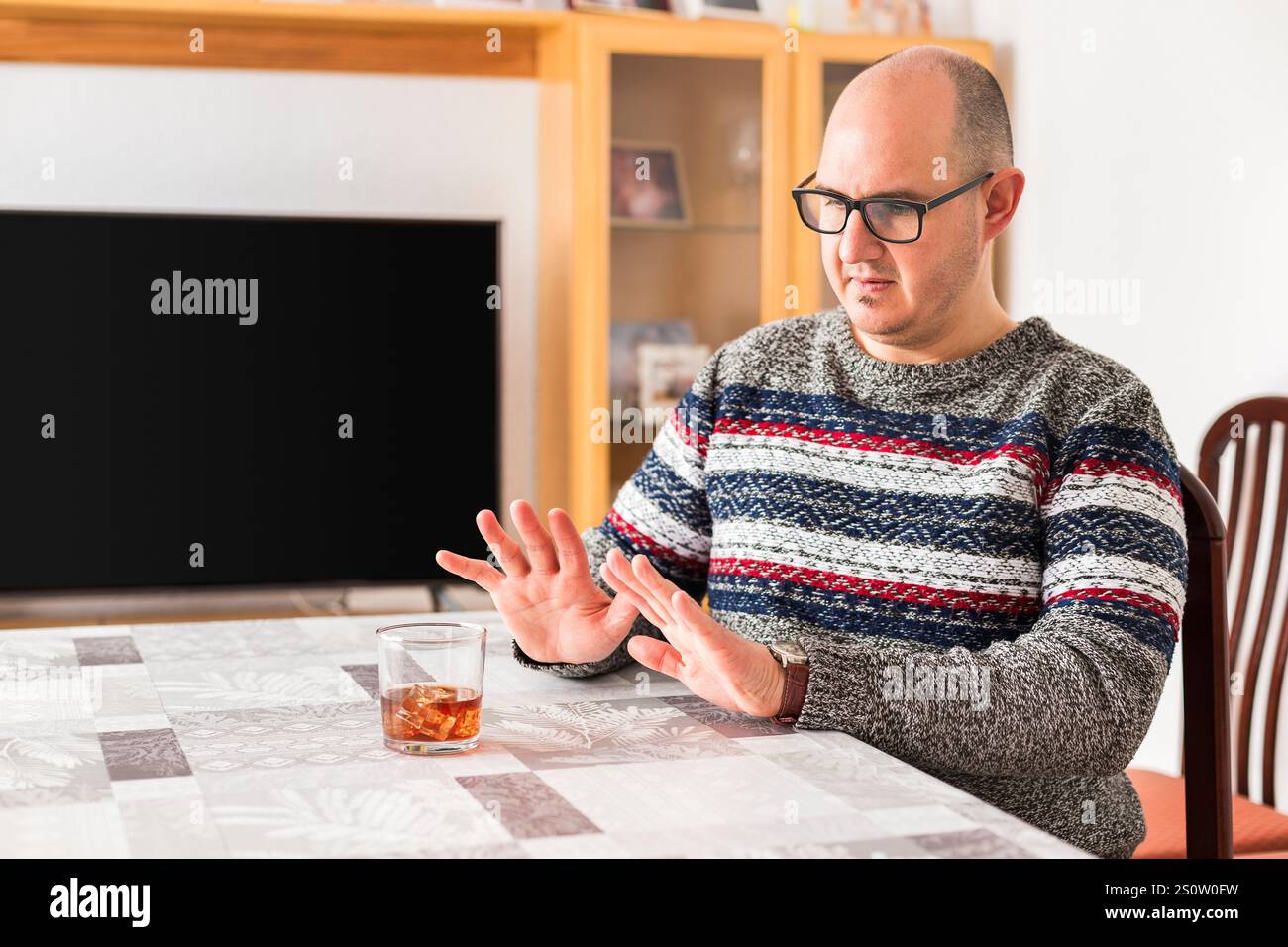 A bald man with glasses sitting next to a table on which there is a ...
