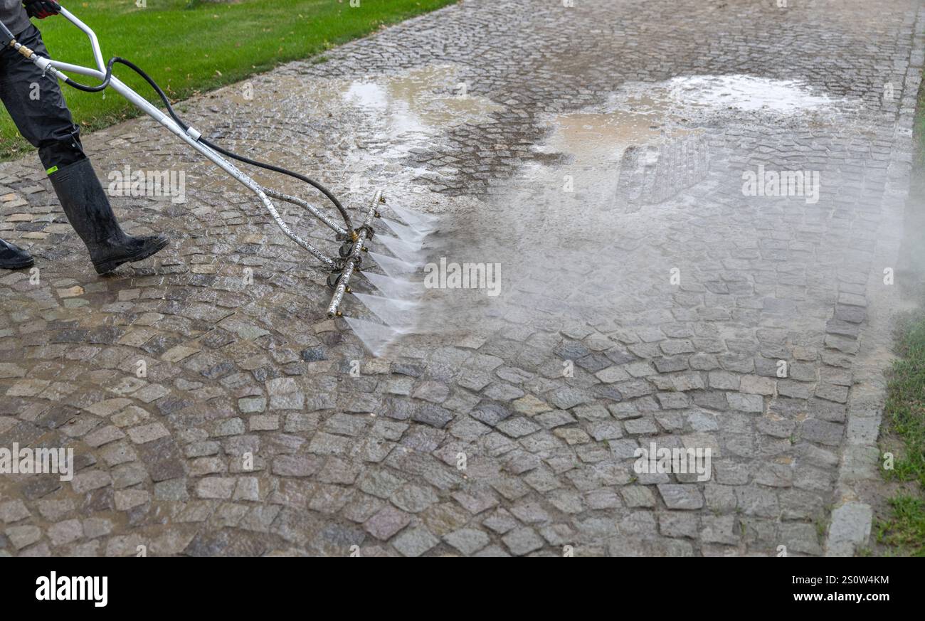 Cleaning service worker washing cobblestone pavement with pressure ...