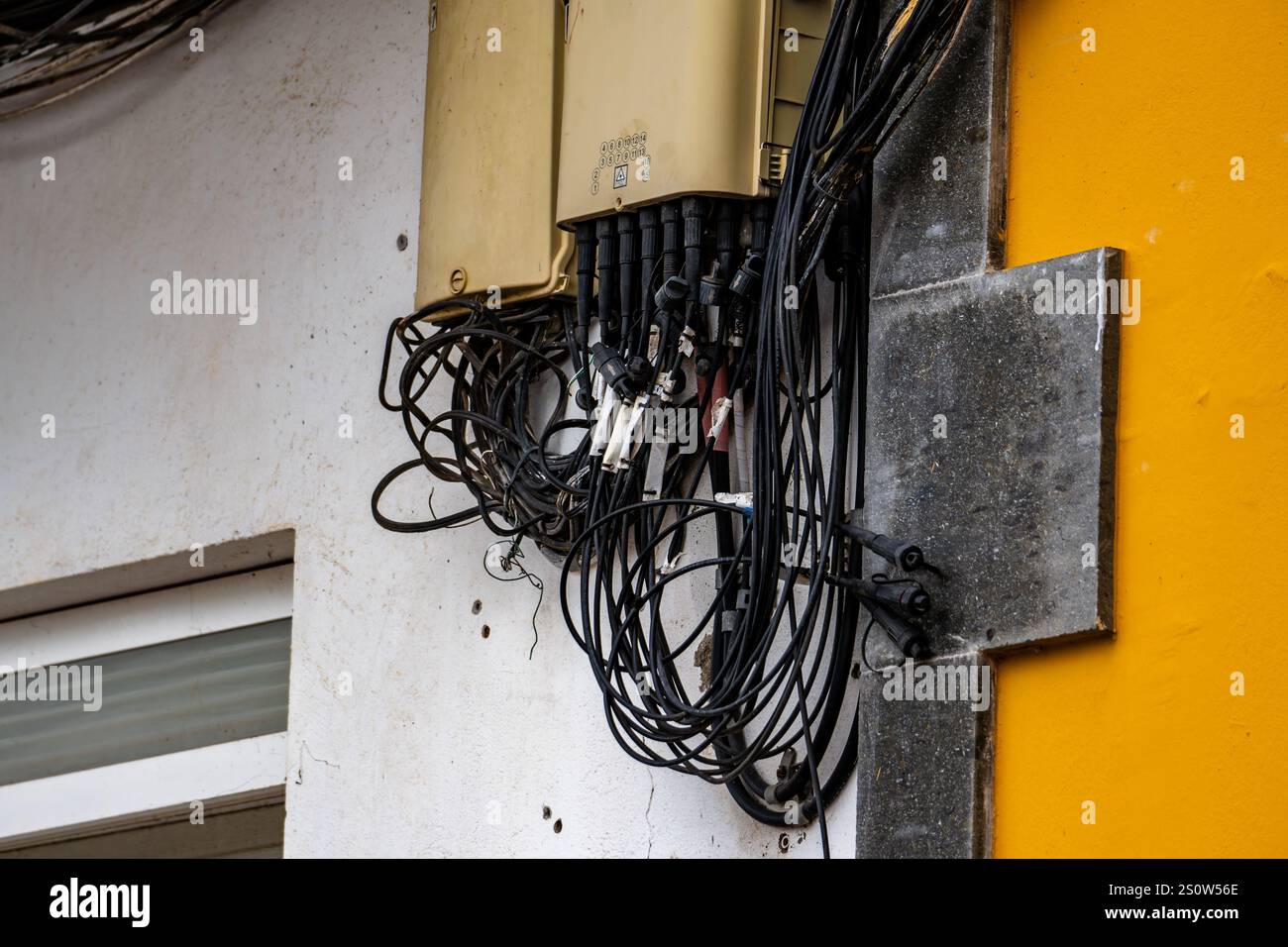 A wall with a bunch of wires hanging from it. The wires are black and ...