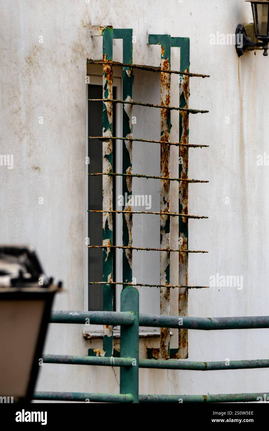 A window with a green frame and a rusty metal bar. The window is dirty ...