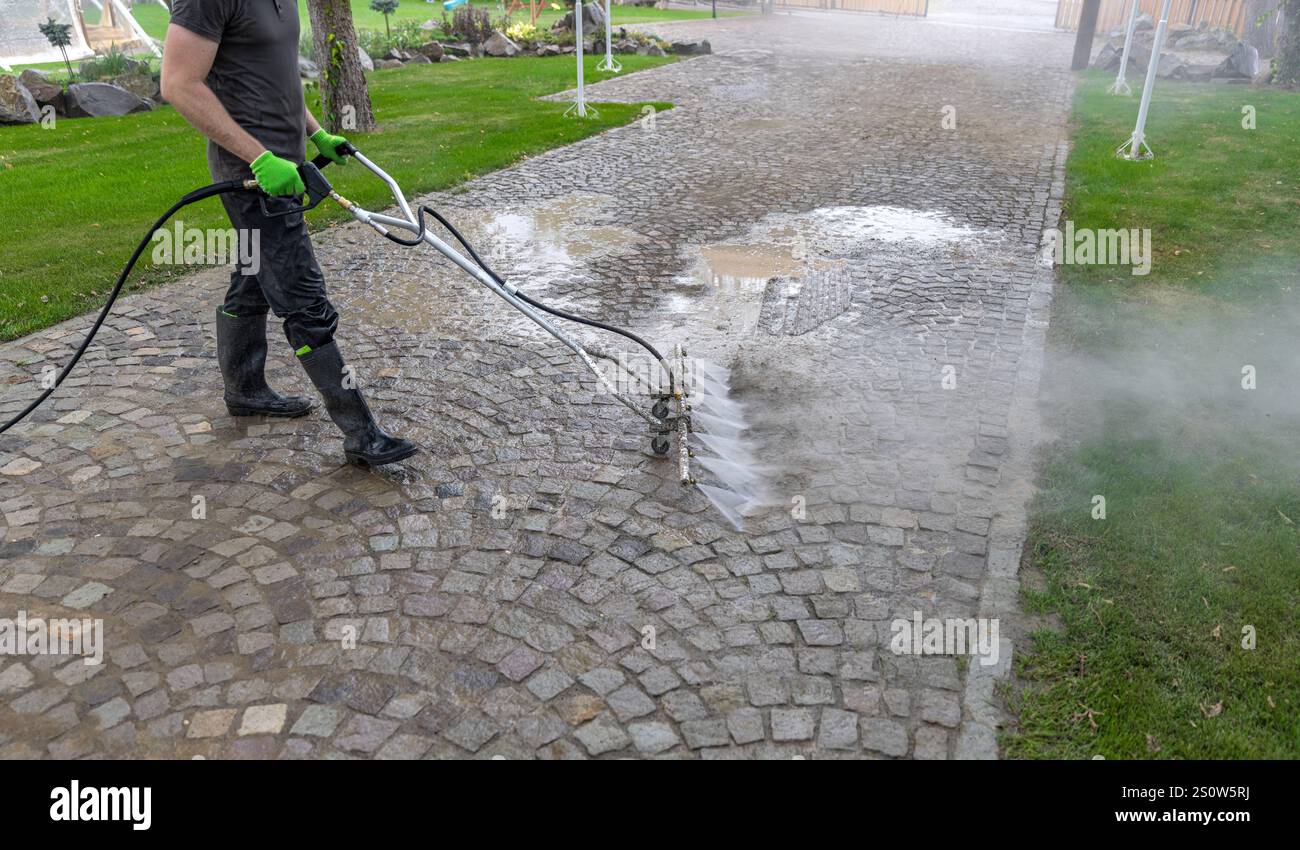 Professional cleaning service worker washing cobblestone pavement using ...