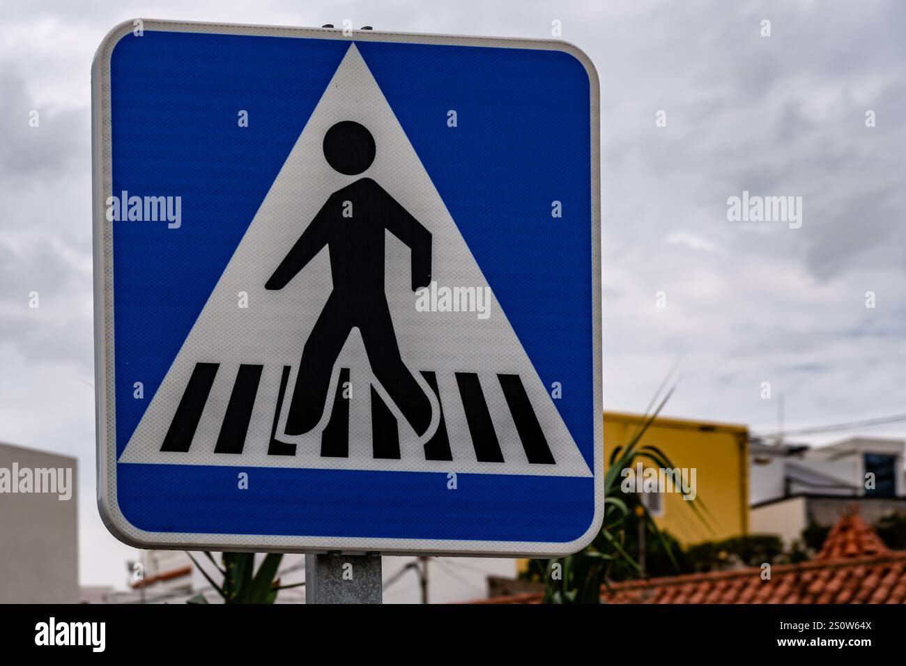 A blue and white sign with a person walking across a crosswalk. The ...