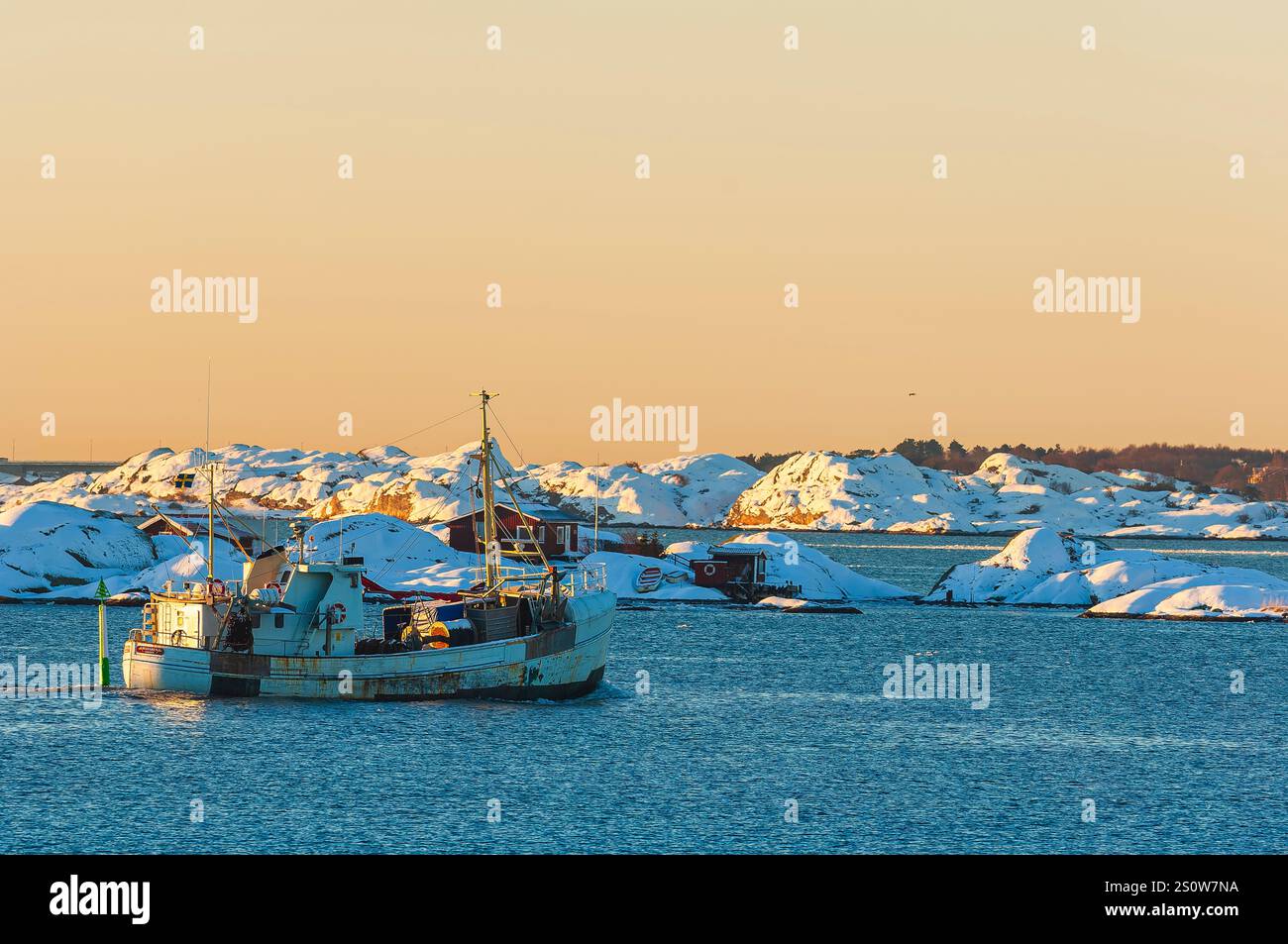 A fishing boat moves through tranquil waters surrounded by snow-covered ...