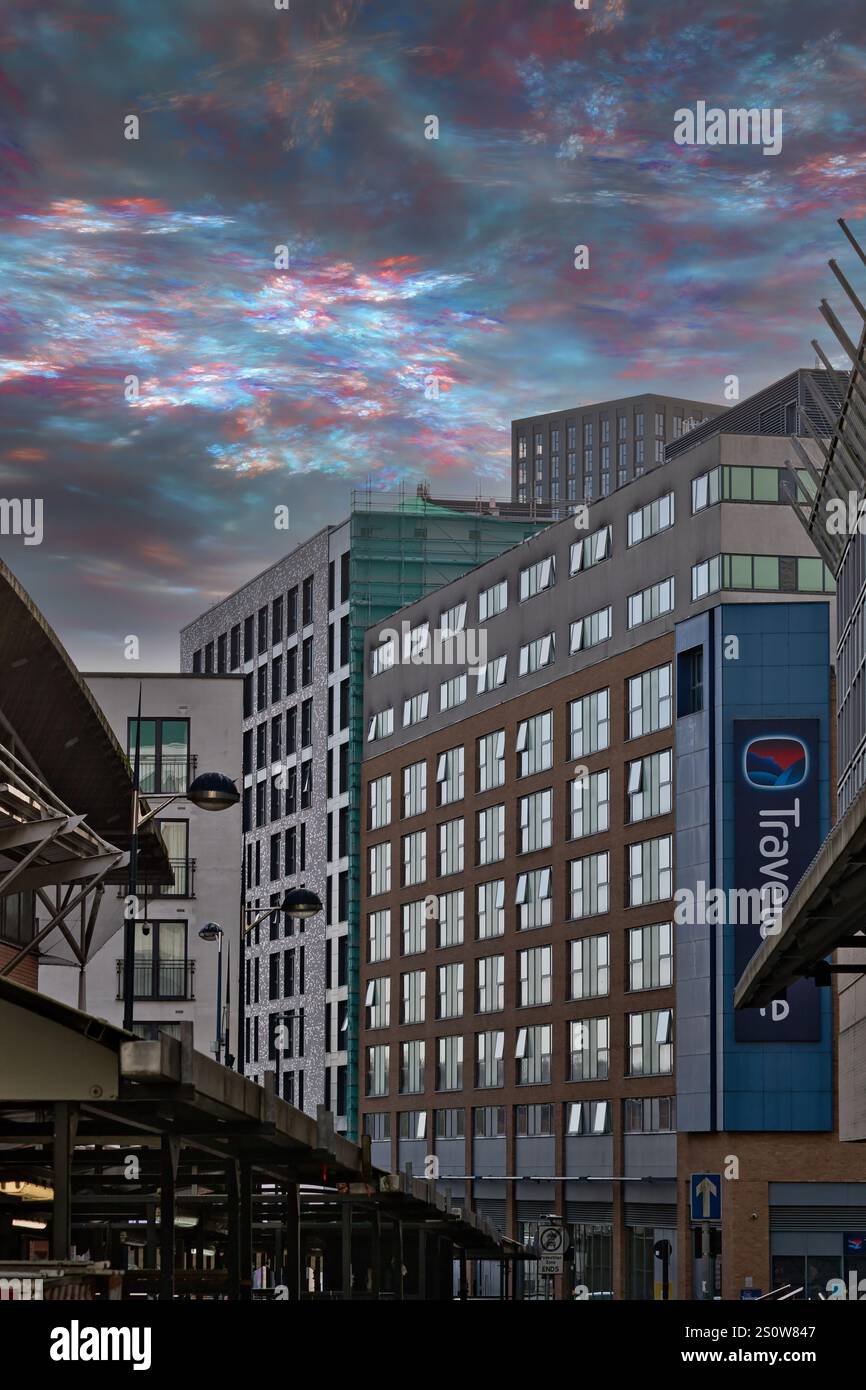 Modern city buildings under a vibrant, colorful sky. A Travelodge sign ...