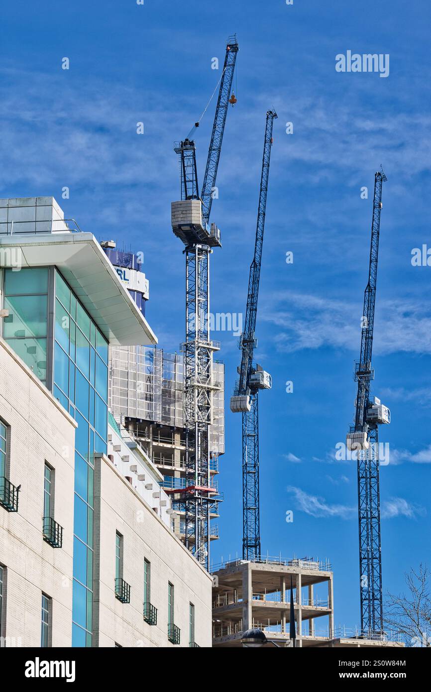 Three tower cranes dominate a construction site, juxtaposed against a partially completed high ...