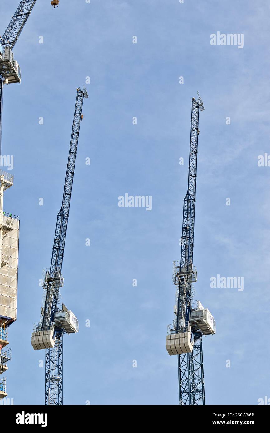 Three tall construction cranes dominate a clear blue sky. Two are ...