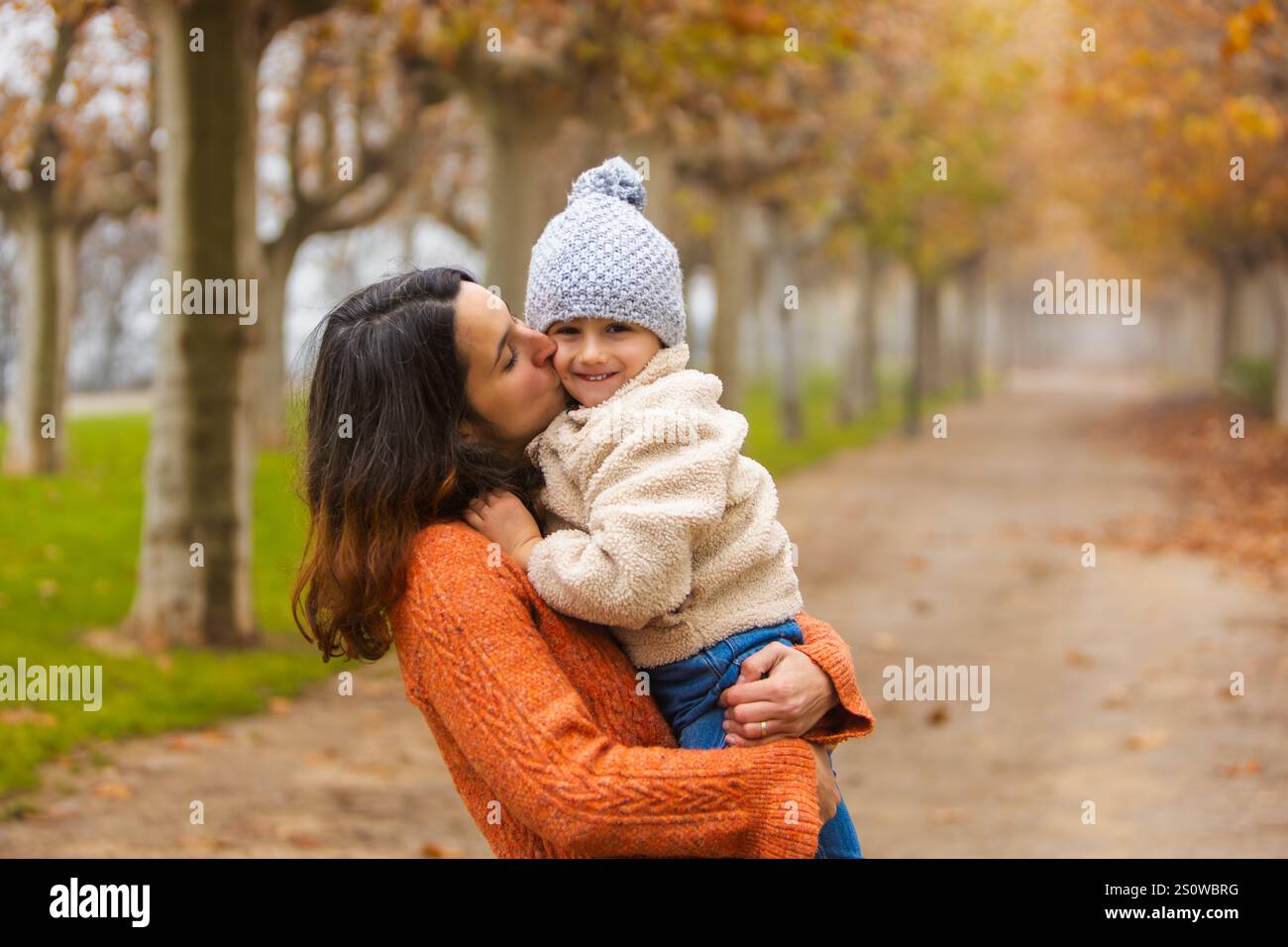Mother kissing her smiling child in a tender autumn moment. Lifestyle. Parenting. Motherhood ...