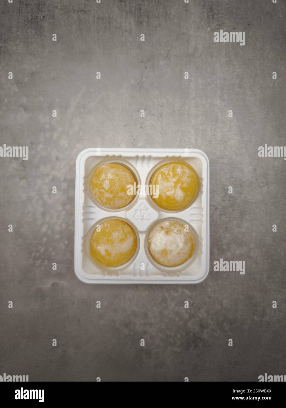 Four mango mochi sit in a plastic container on a marble countertop ...