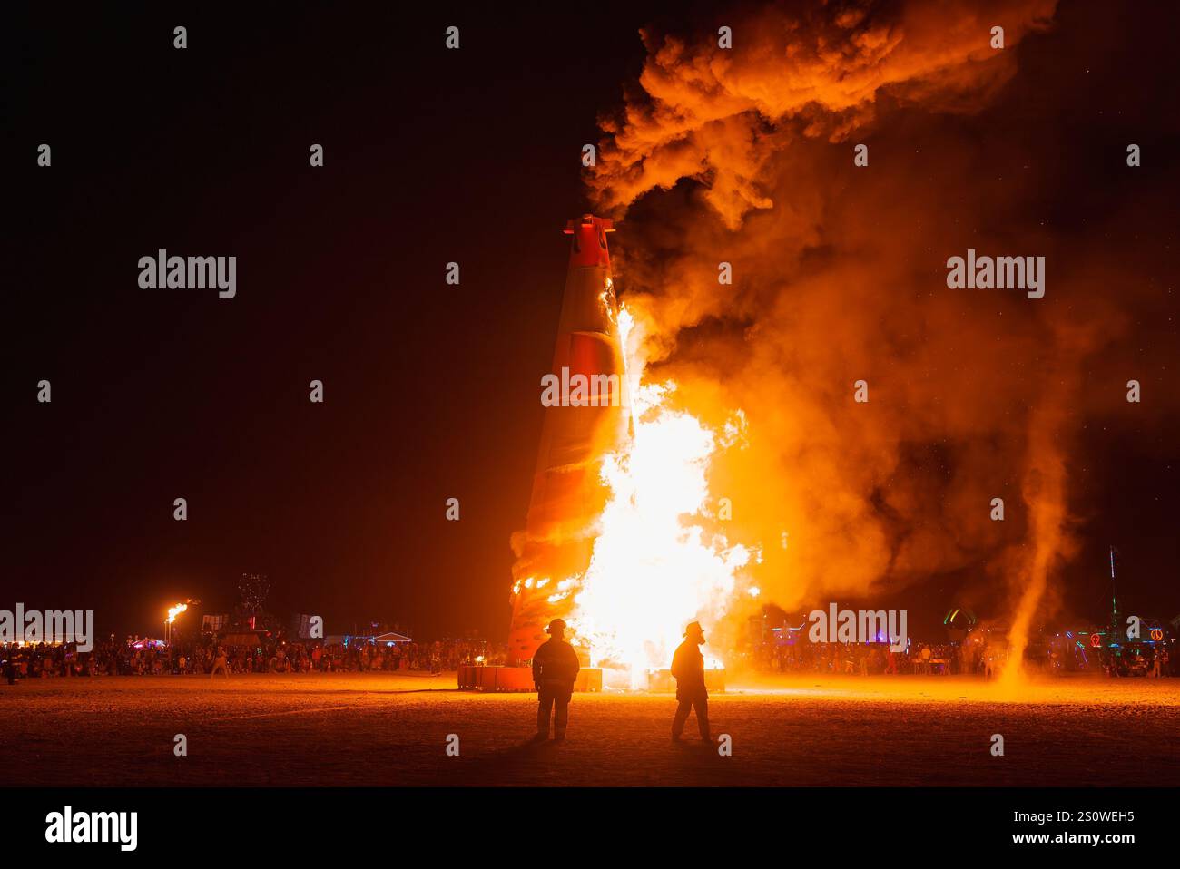 A large cone shaped structure burns brightly at a desert festival ...