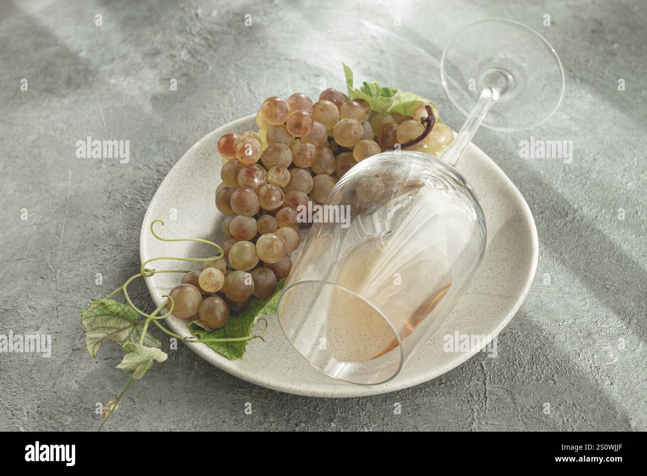 A branch of white grapes, on a gray plate, with a glass of white wine, top view, natural light ...