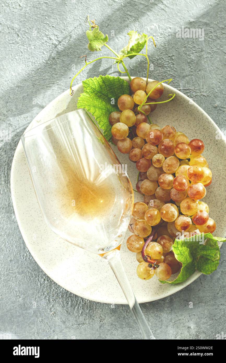 A branch of white grapes, on a gray plate, with a glass of white wine, top view, natural light ...