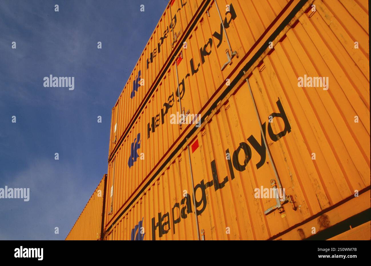Yellow freight containers from Hapag-Lloyd pile up under a blue sky ...