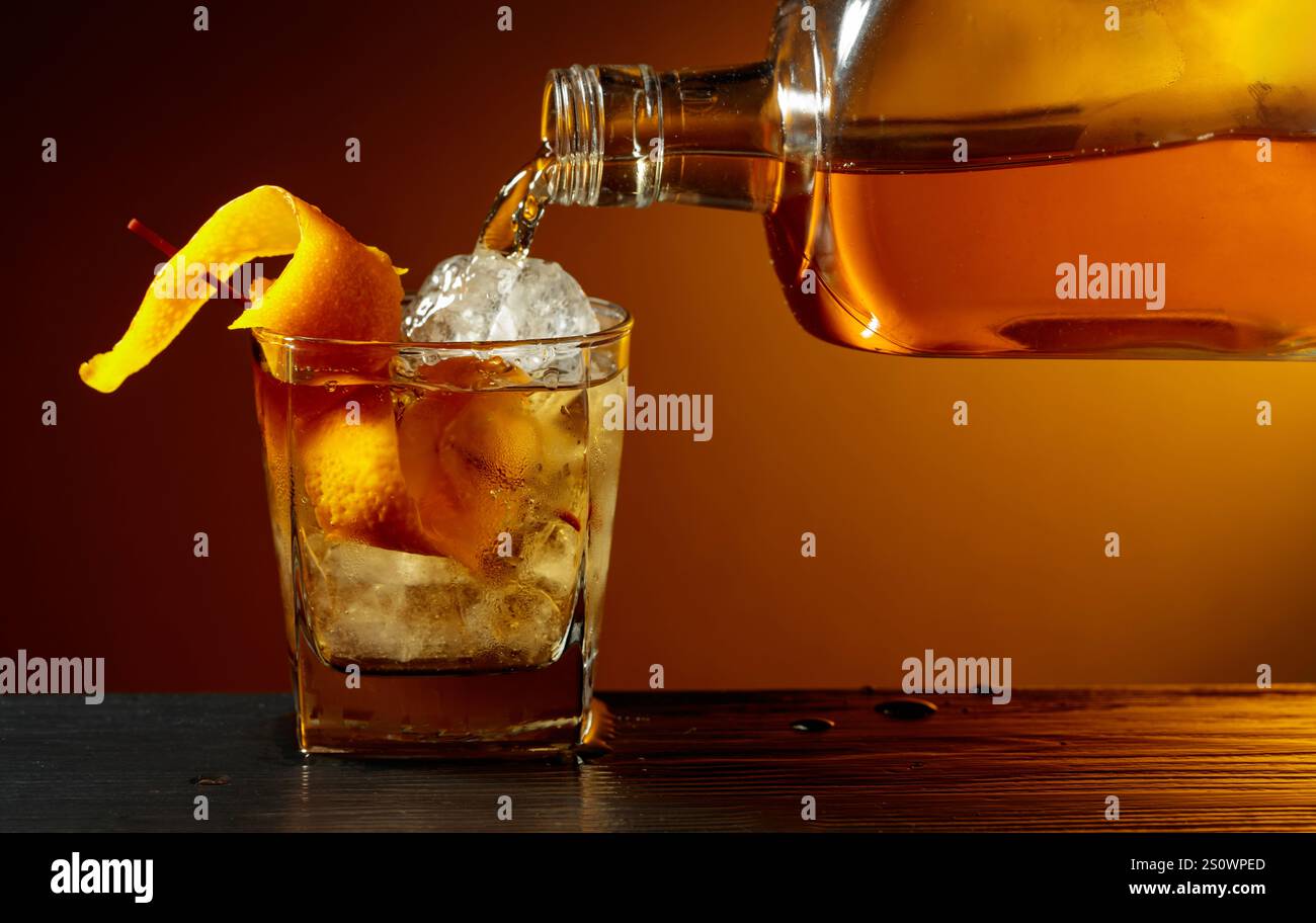 Whiskey or bourbon pouring into a glass. Glass with whiskey and ice cubes, garnished with an ...