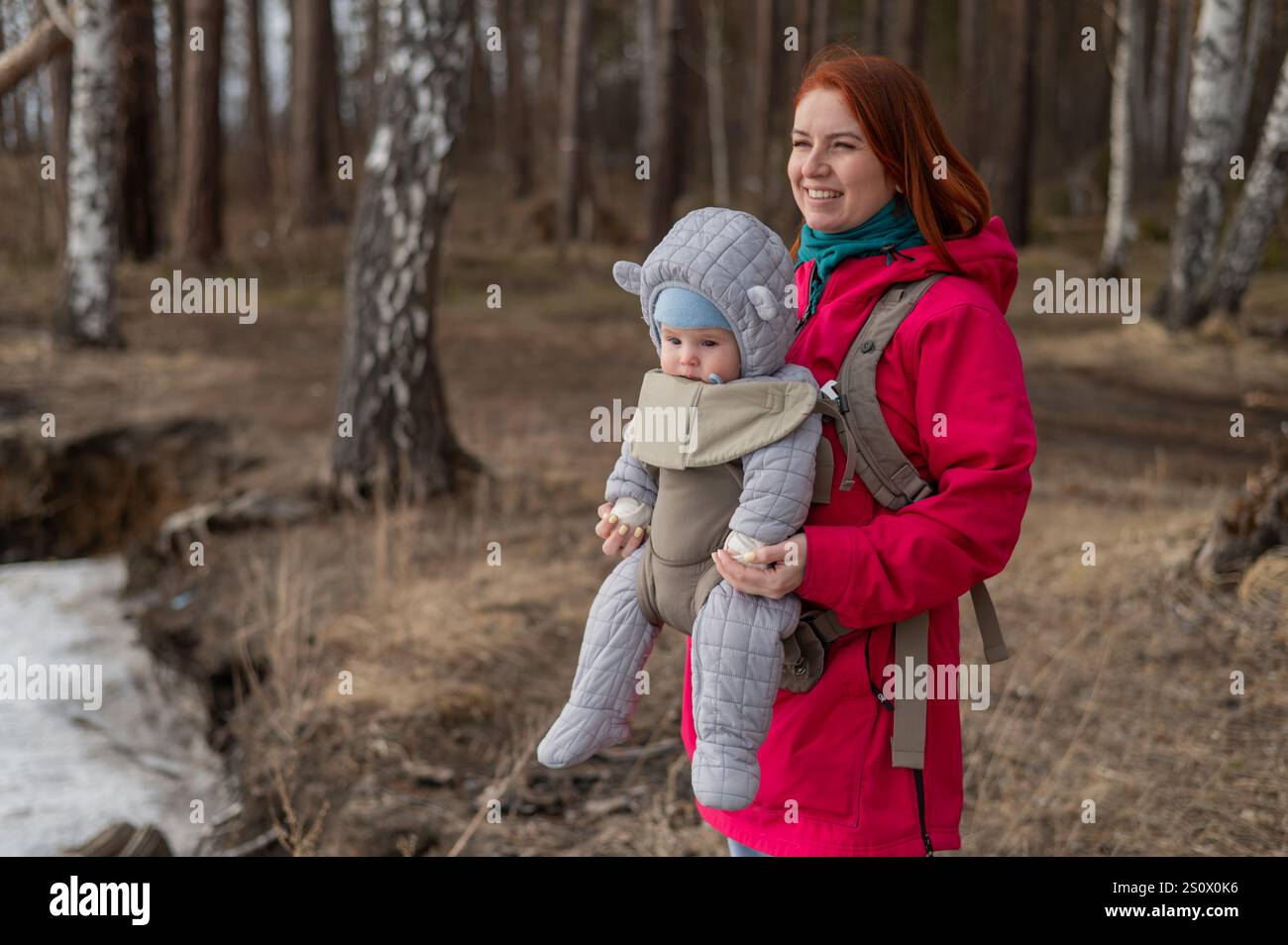 Caucasian red-haired woman walks with her son in an ergo backpack in nature in winter Stock ...