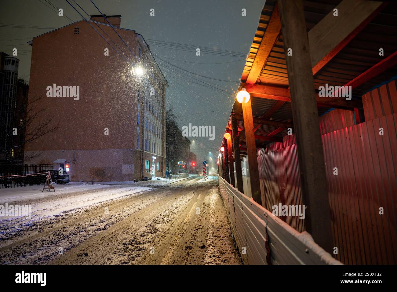 Snowy residential street at night, slush accumulating on illuminated ...