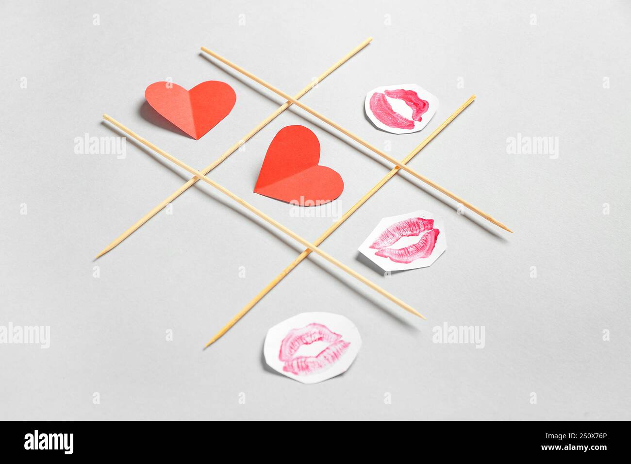 Tic tac toe game with paper hearts and lipstick kiss marks on light ...