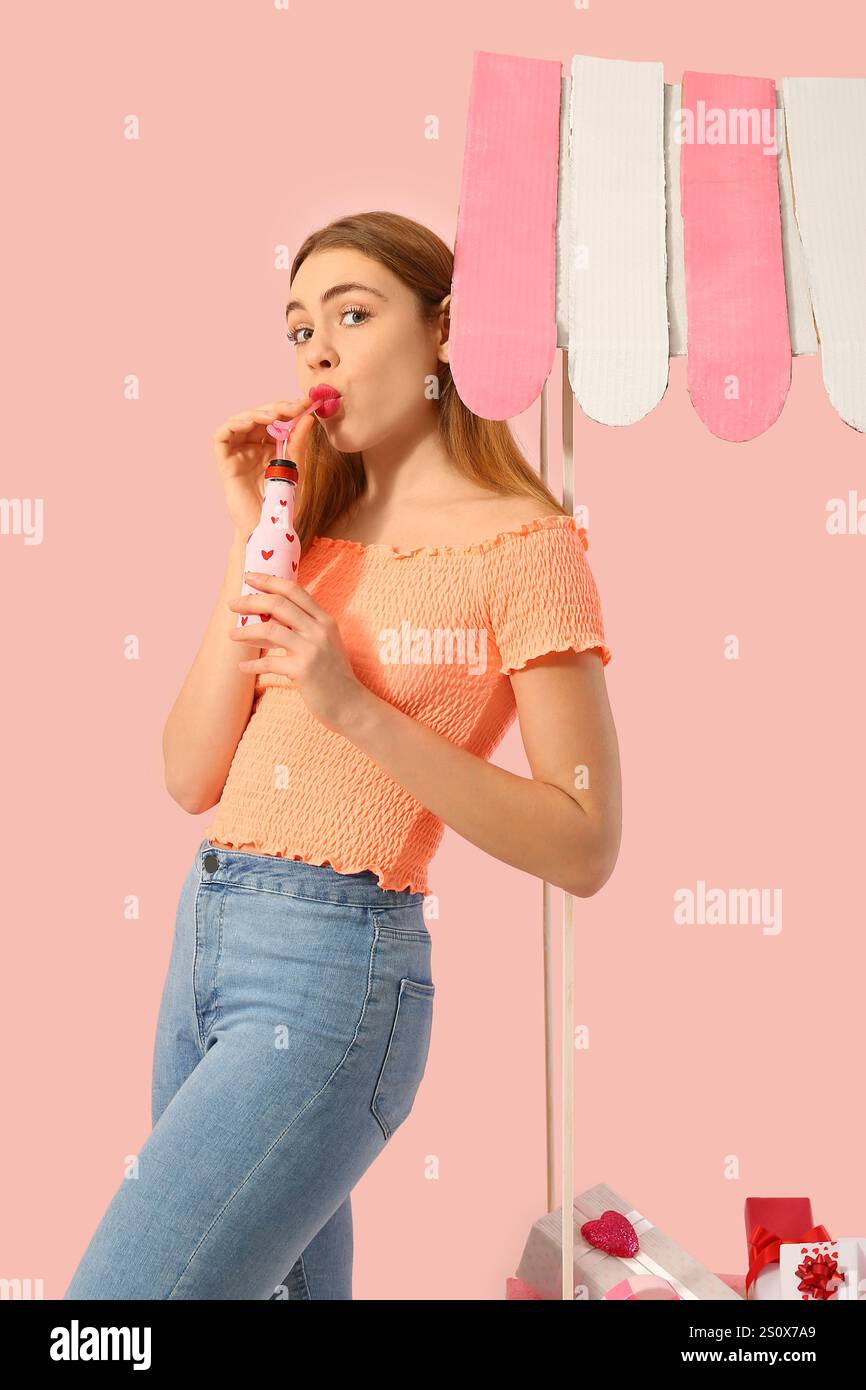 Young woman drinking soda and paper booth near pink wall. Valentine's Day celebration Stock ...