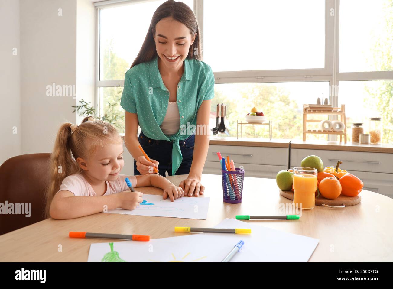 Nanny with cute little girl drawing in kitchen Stock Photo - Alamy