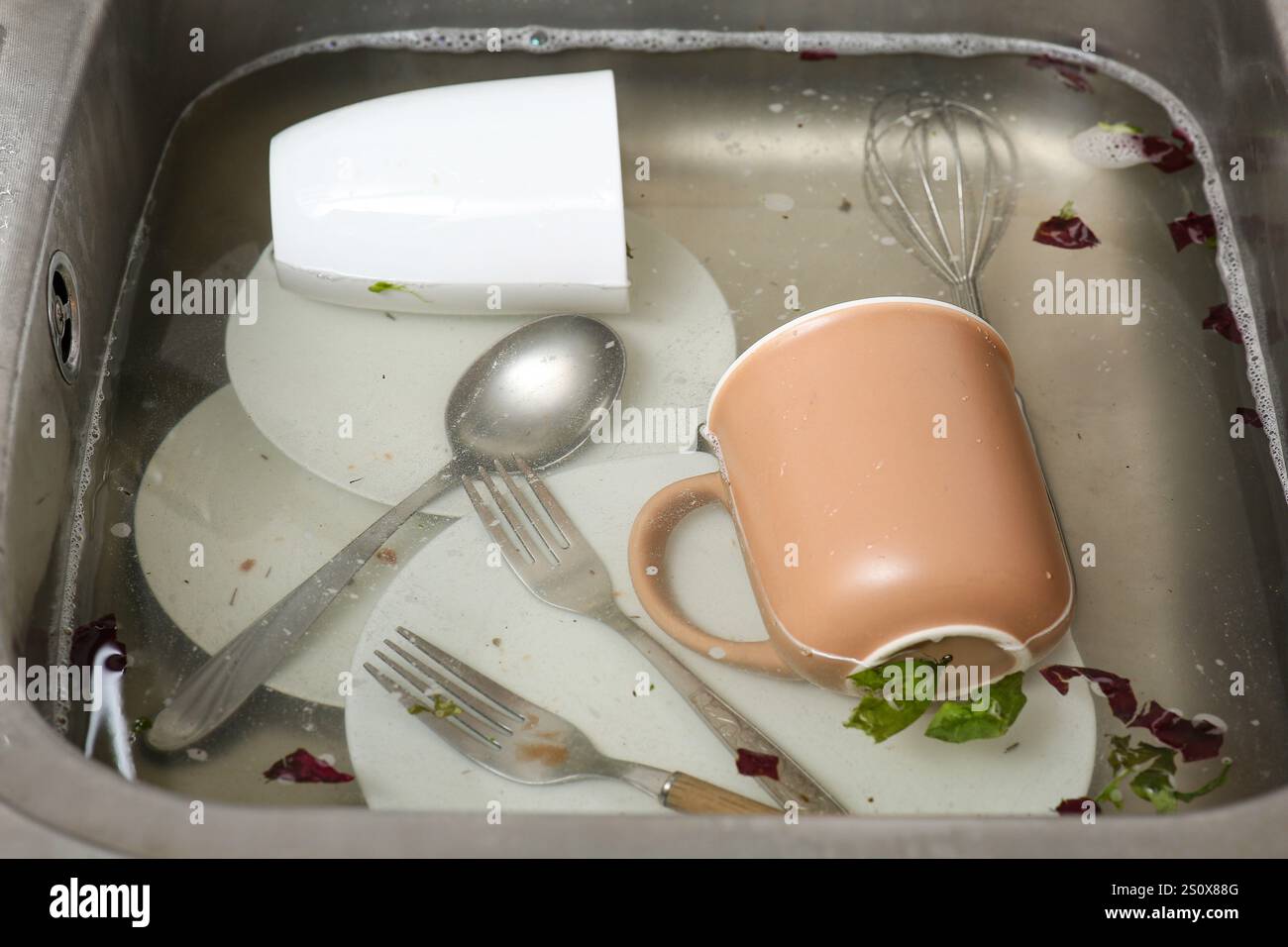 Metallic kitchen sink with soap water, dirty dishes and food leftovers ...
