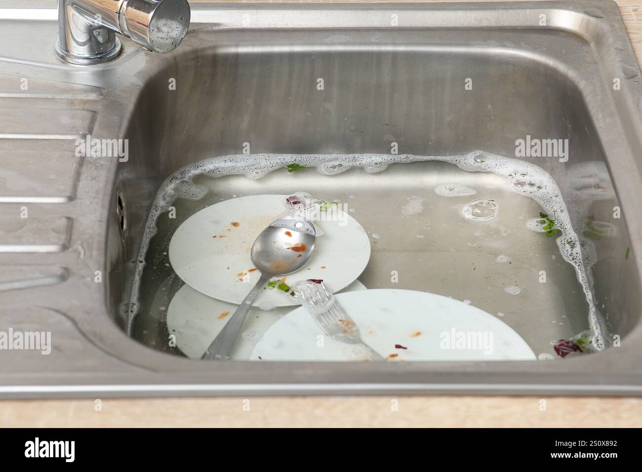 Metallic kitchen sink with dirty dishes, soap water and food leftovers ...