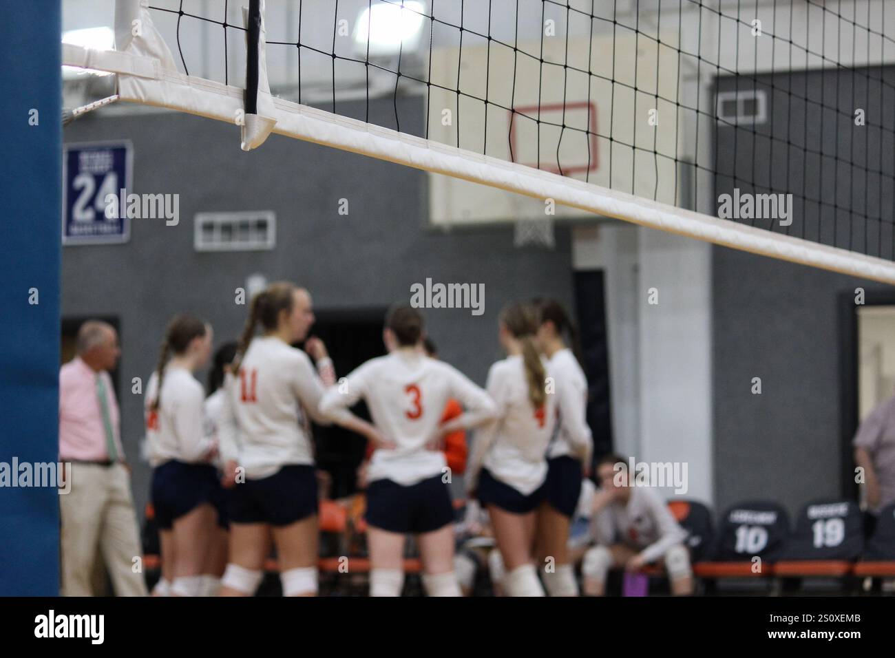Volleyball net with high school girls' volleyball team huddling in the ...