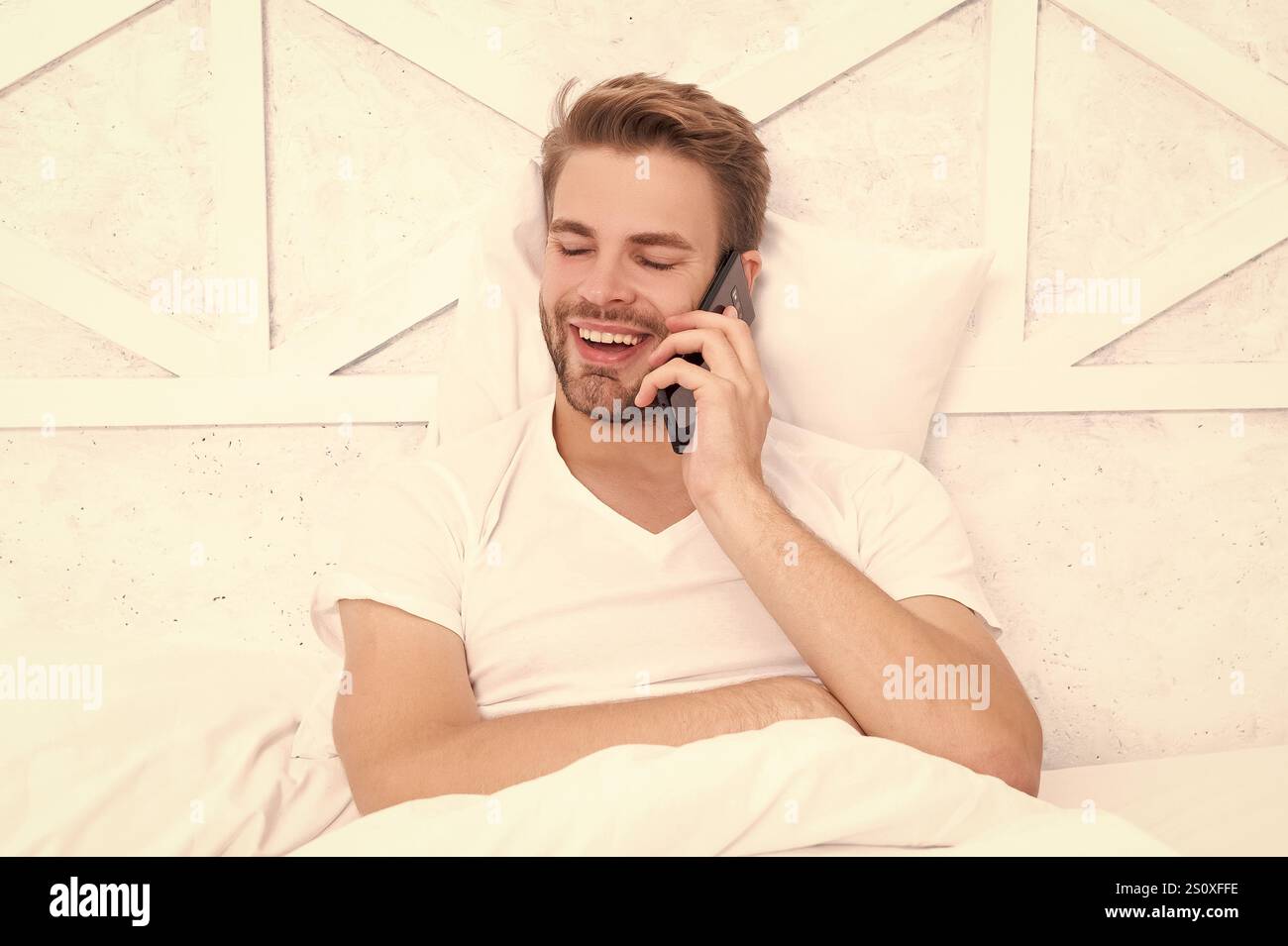 Young man in bed having phone conversation. Phone call. Man with smartphone in bed. Smartphone ...