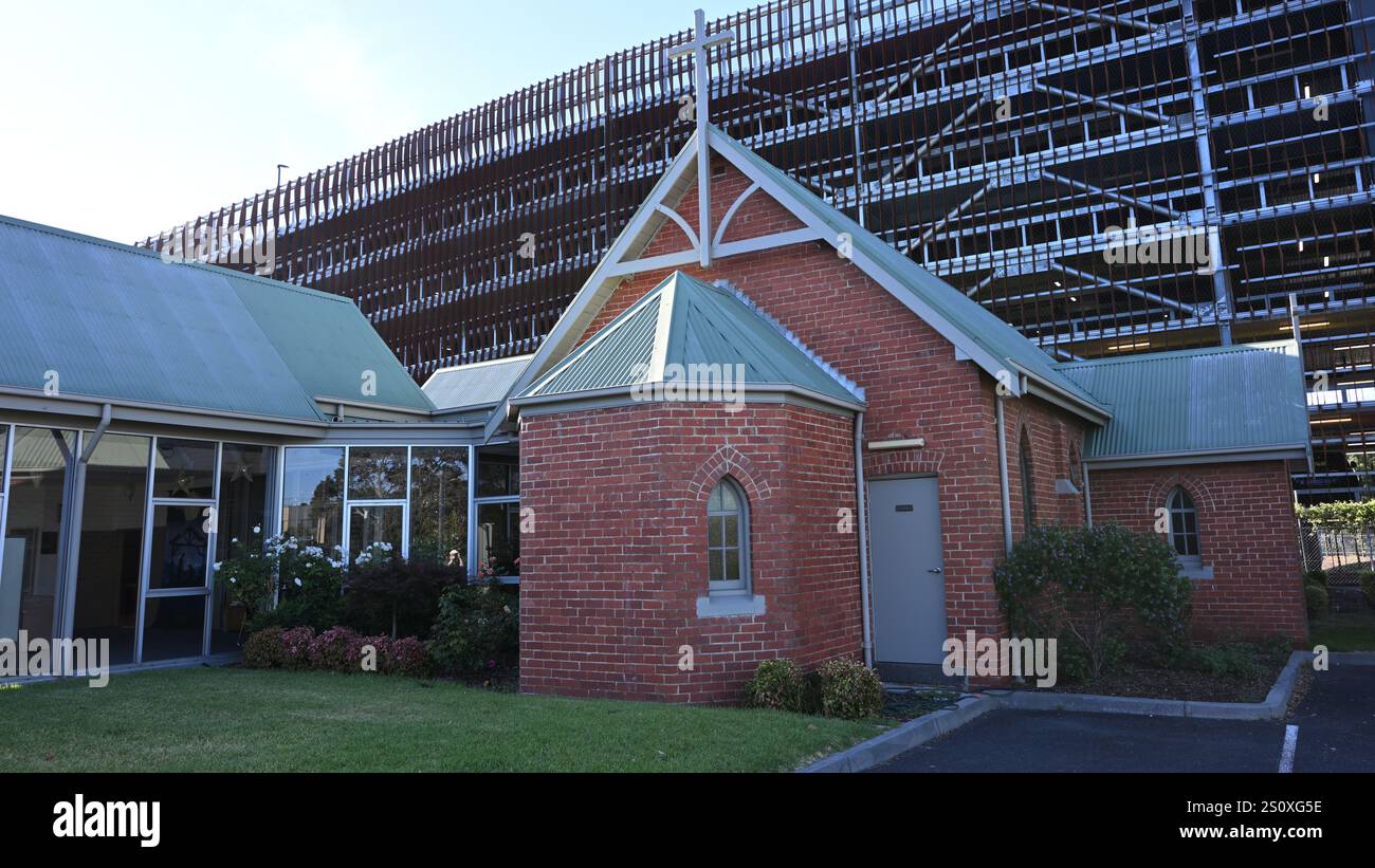 Modest red brick Anglican church overshadowed by large metallic carpark ...
