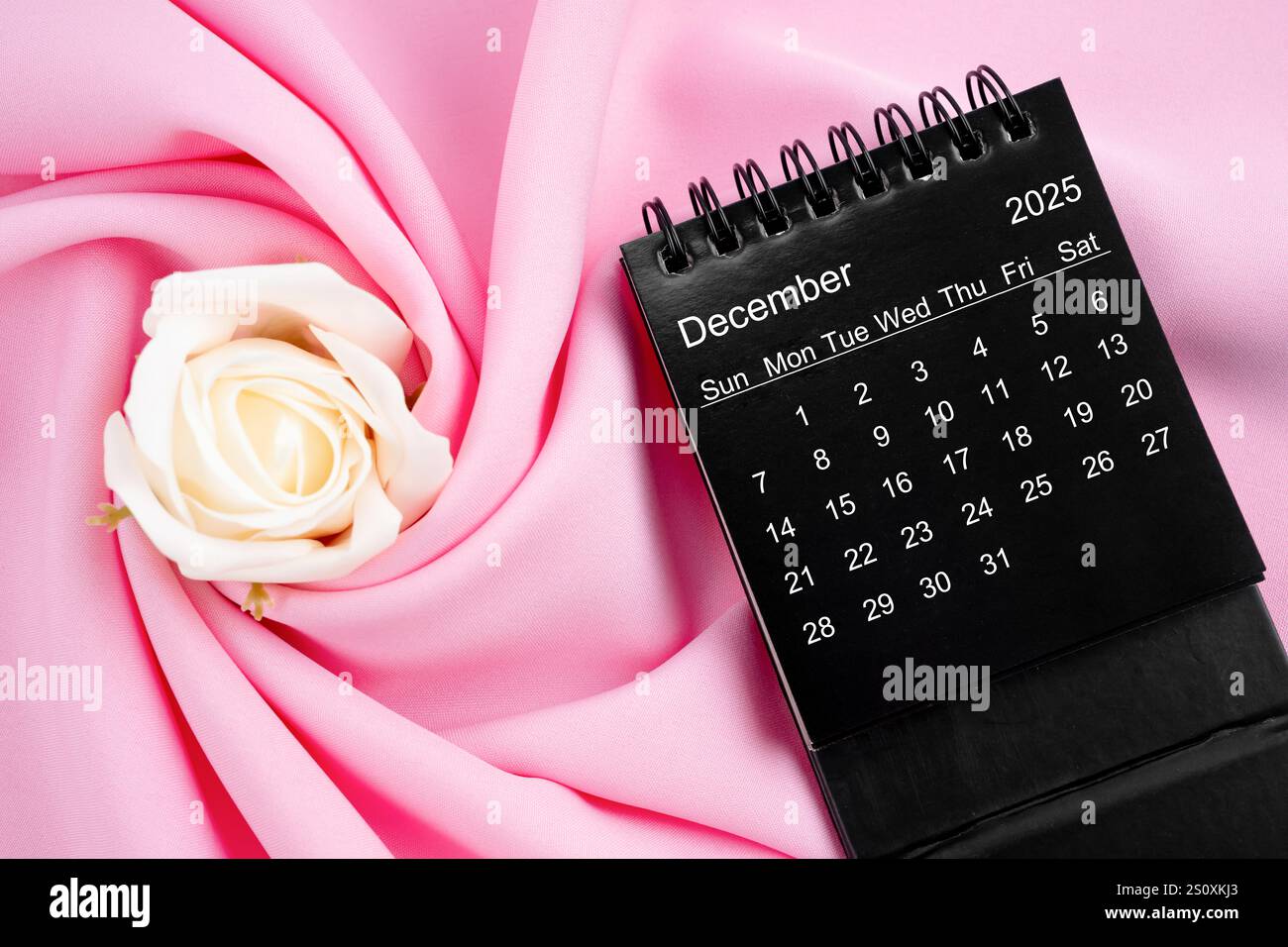 December 2025 desk calendar black color and rose on pink textile ...