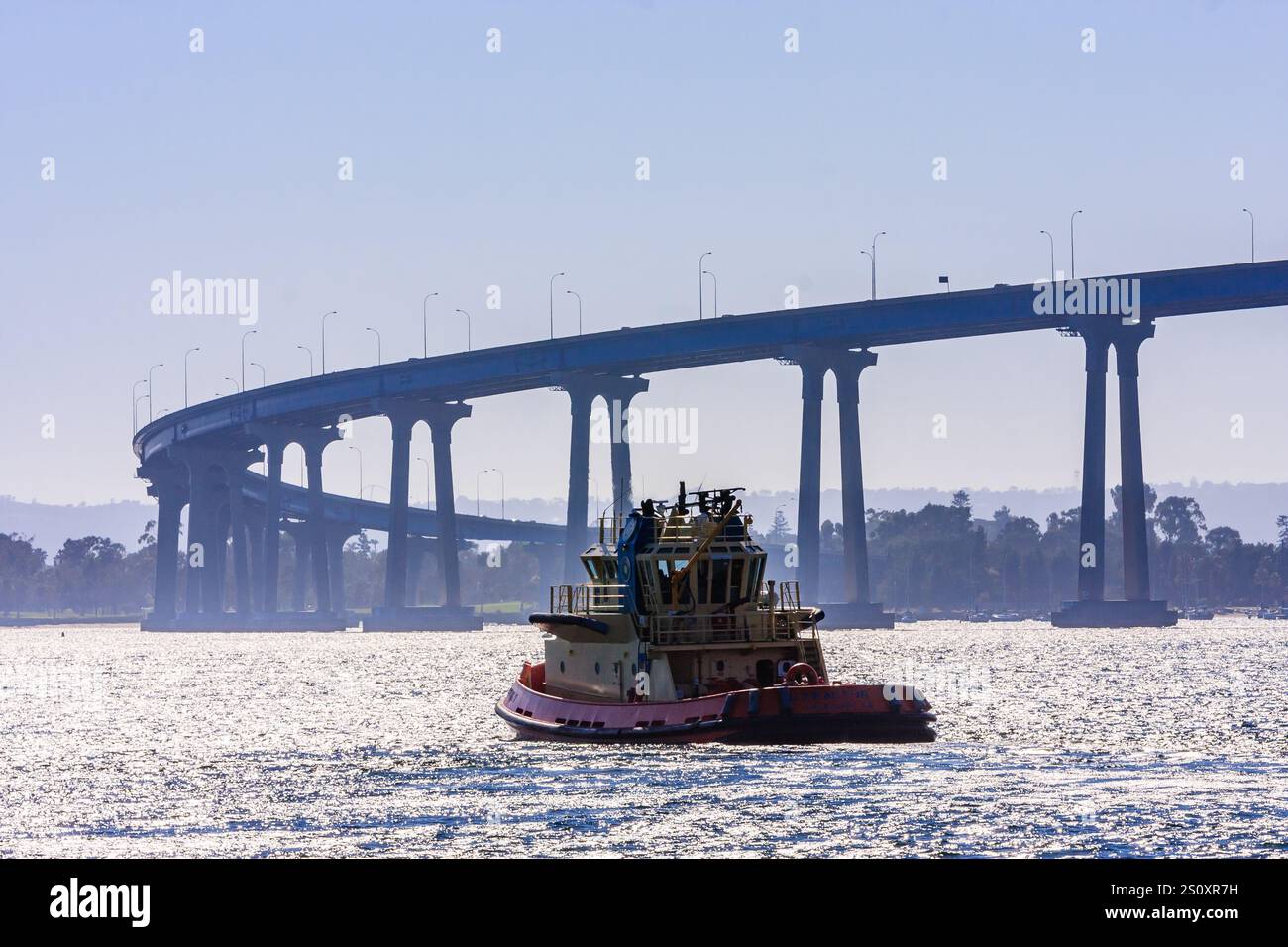 A large tugboat is on the water near a bridge. The sky is clear and the ...