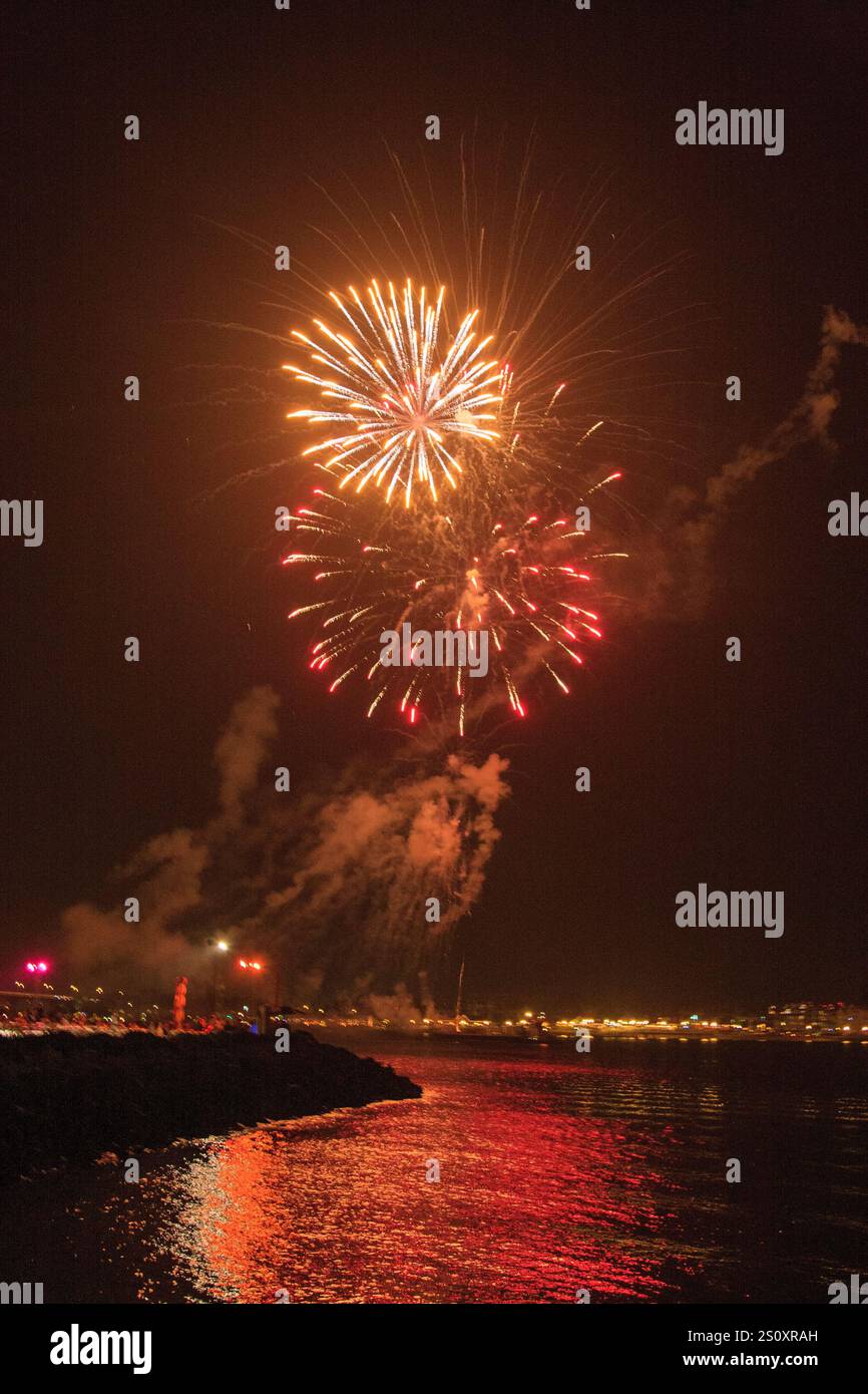 A fireworks display is lit up in the night sky over a body of water ...