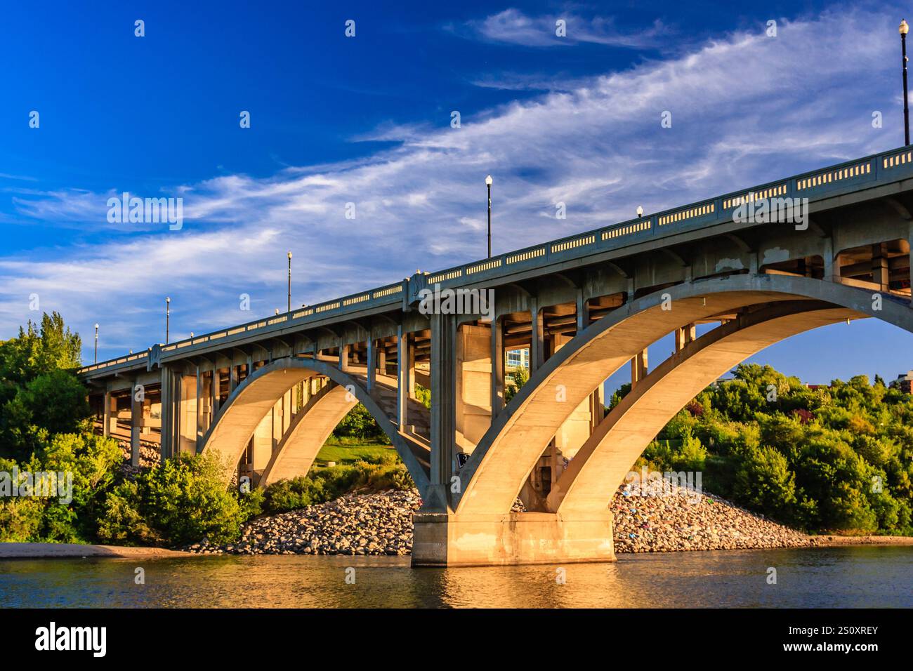 A bridge spans a river with a clear blue sky above. The bridge is made ...