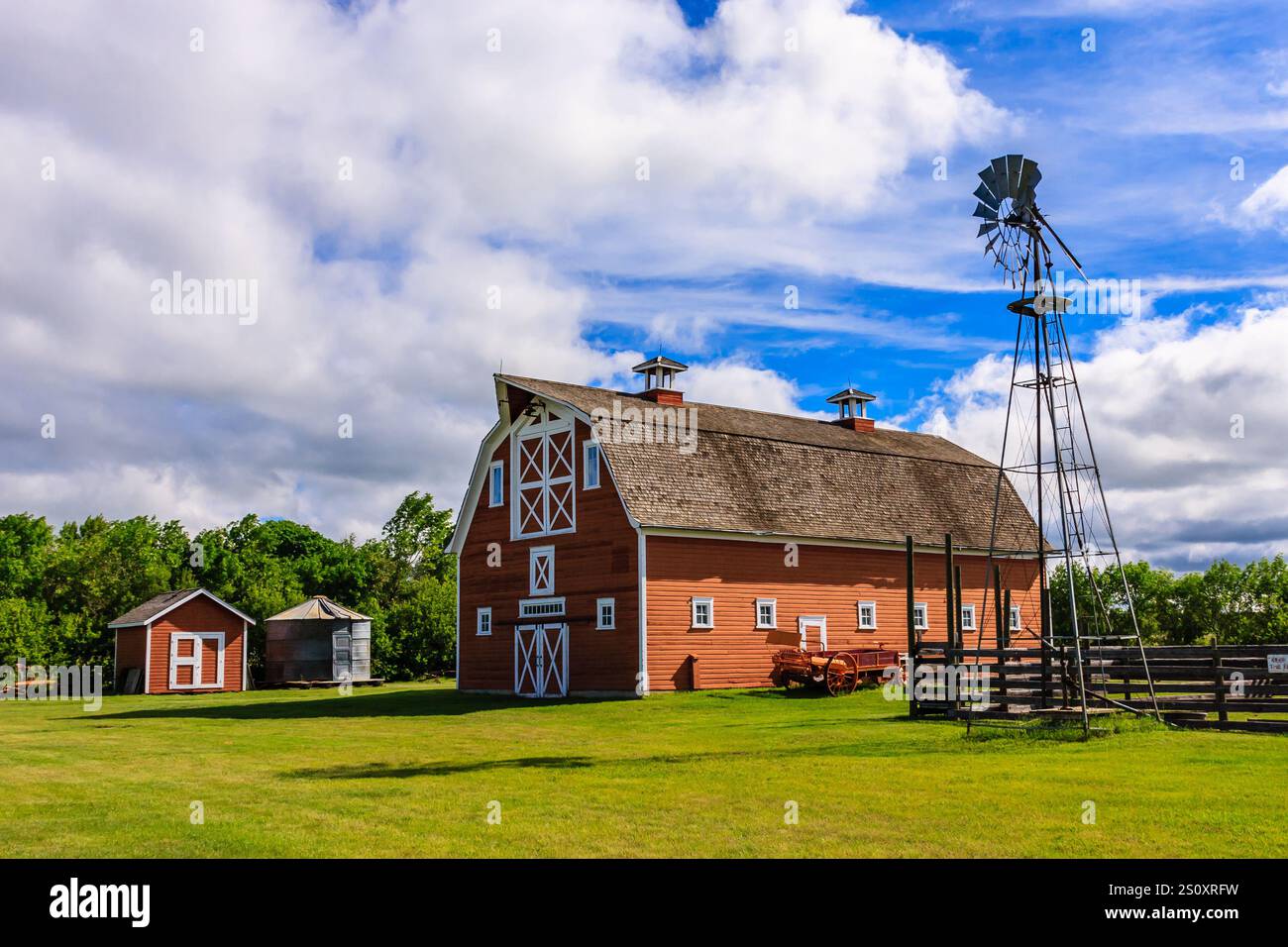A red barn with a windmill on top stands in a field. The barn is ...