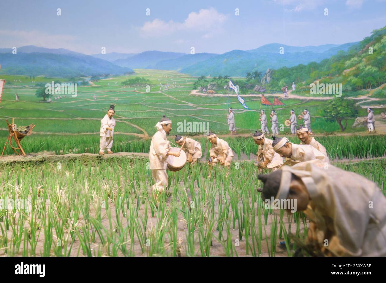Villagers playing music on drums in the village, fields. A diorama at ...
