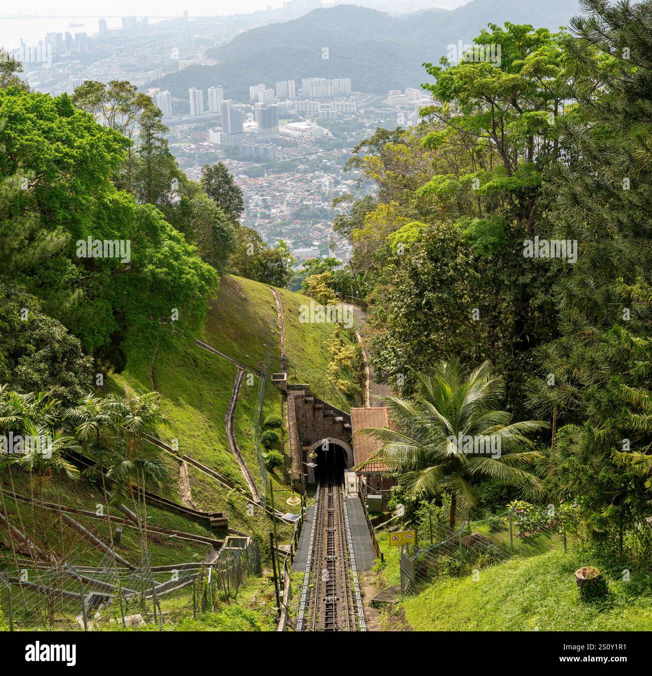 Funicular railway on Penang Hill, track leading into tunnel surrounded by lush greenery ...