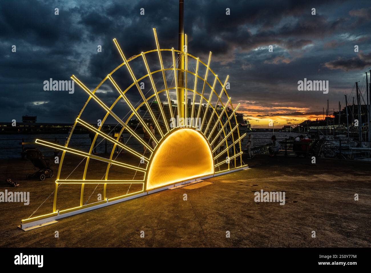 A glowing art installation resembling the sun highlights a marina with ...