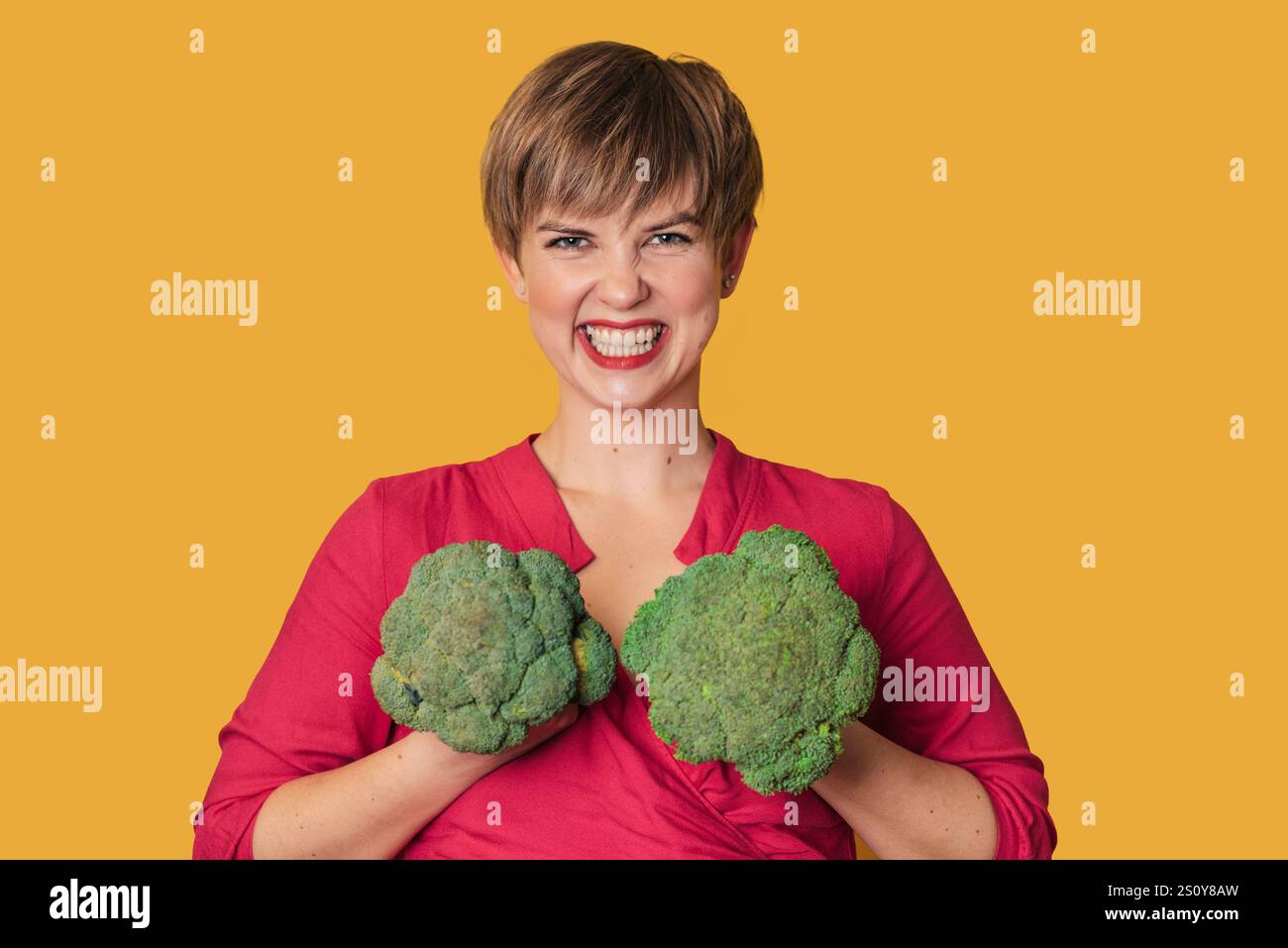 Broccoli in the hand of a slender smiling woman on a yellow background ...