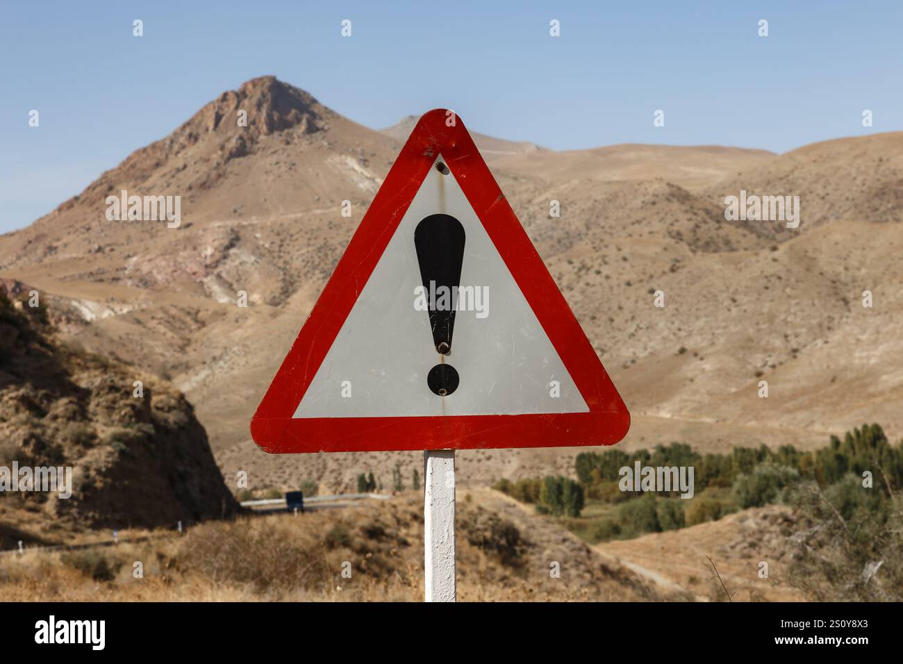 A red and white caution sign stands prominently in a dry mountainous ...