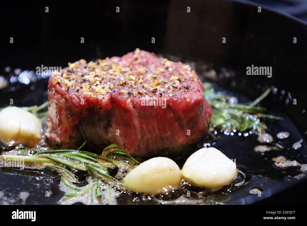 Seasoned filet steak searing with garlic and rosemary in a skillet ...