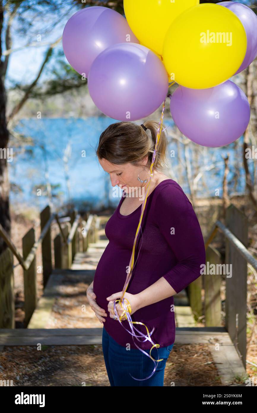 Pregnant woman looks down while holding her belly and balloons Stock ...