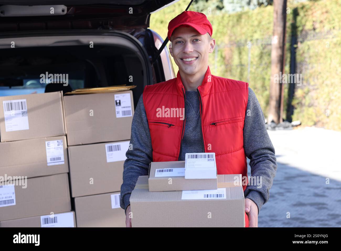 Happy postman with parcels near car outdoors Stock Photo - Alamy