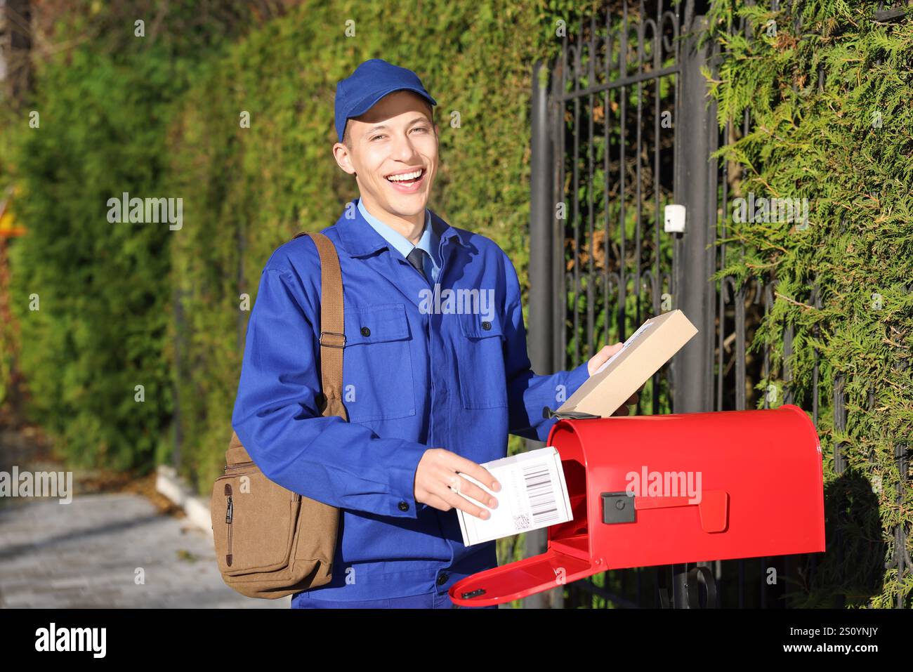 Postman putting parcel into mail box outdoors Stock Photo - Alamy