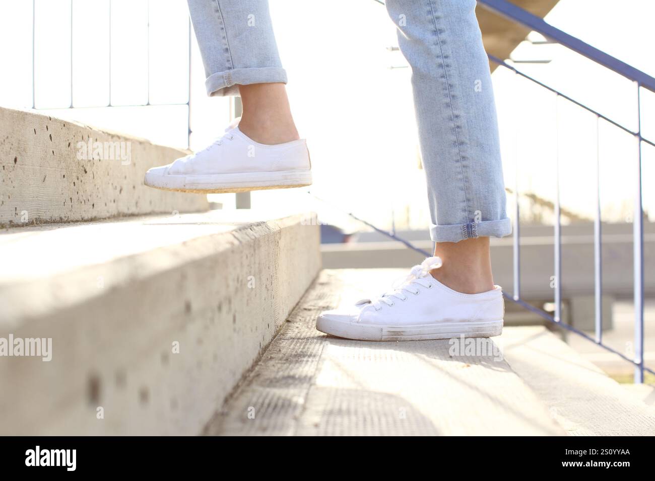 This is a close-up photo of a woman wearing white trainers and jeans ...