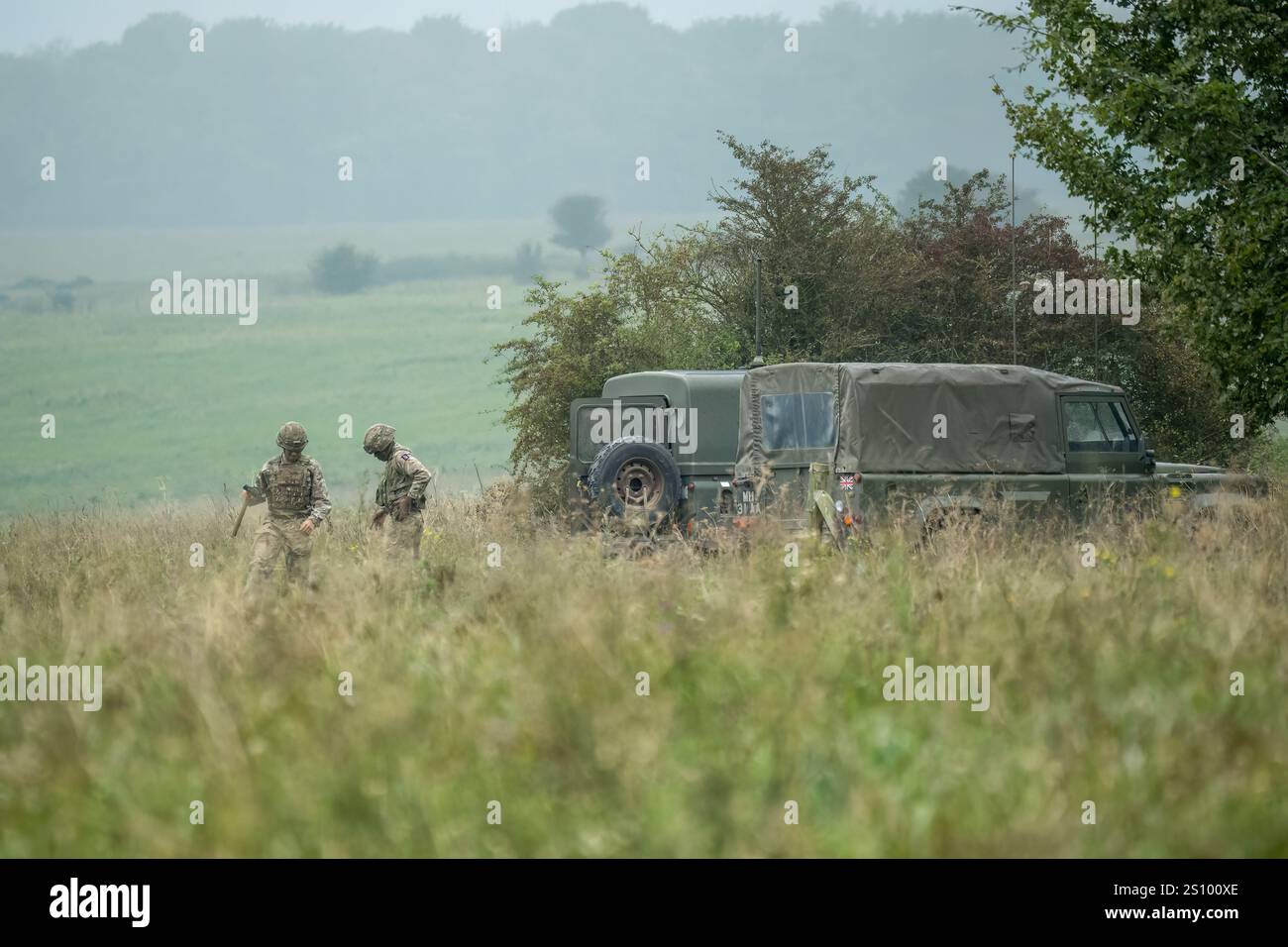 British army soldier prepares a field radio aerial mast, near two Land ...