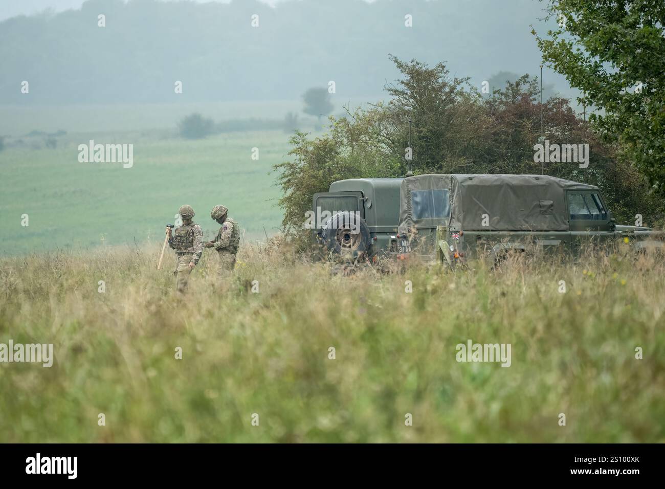 British army soldier prepares a field radio aerial mast, near two Land ...