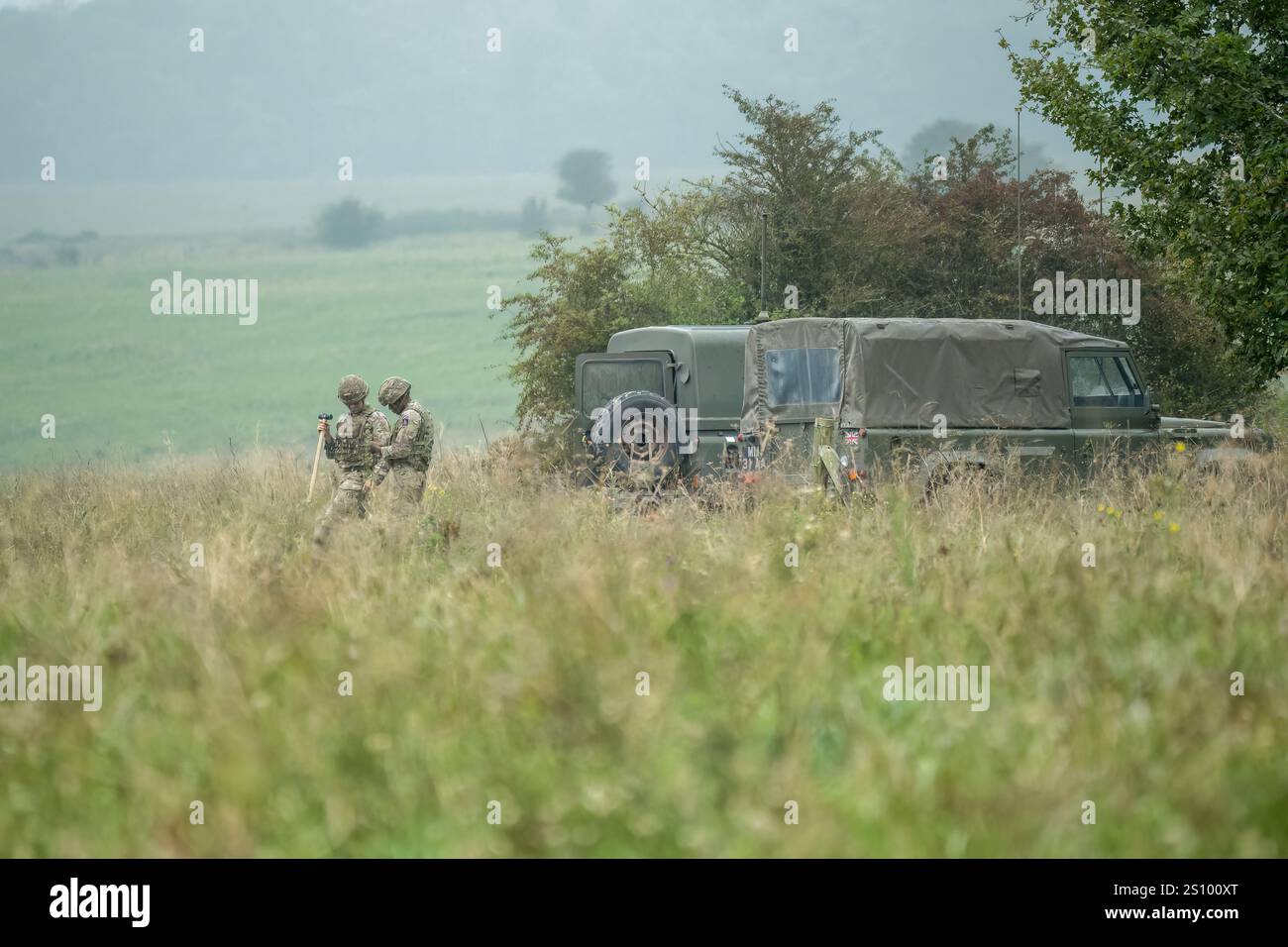 British army soldier prepares a field radio aerial mast, near two Land ...