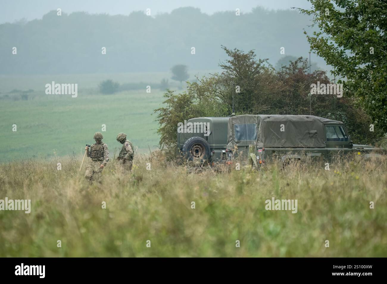 British army soldier prepares a field radio aerial mast, near two Land ...