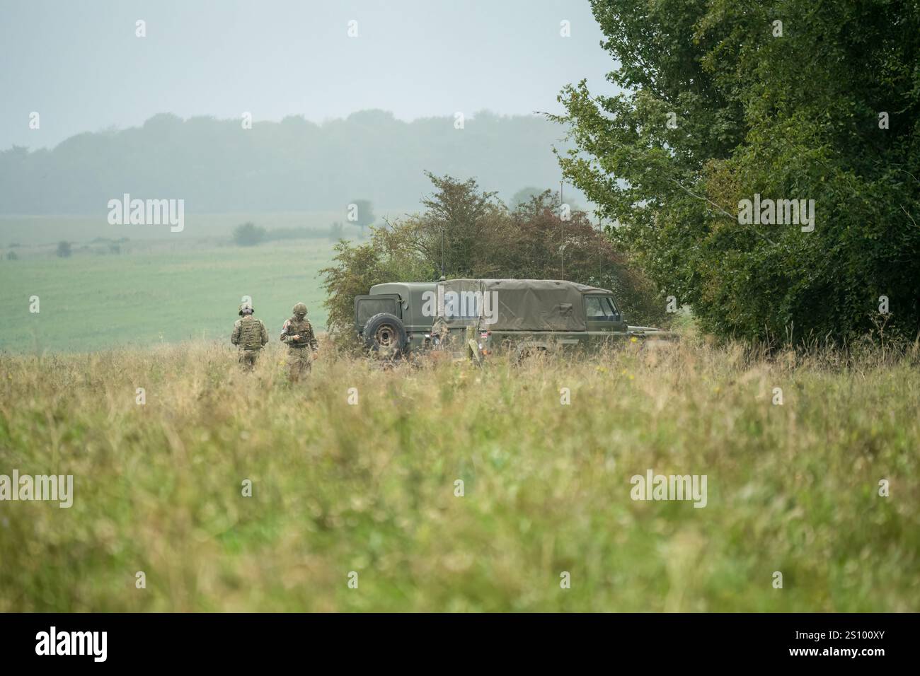 British army soldier prepares a field radio aerial mast, near two Land ...