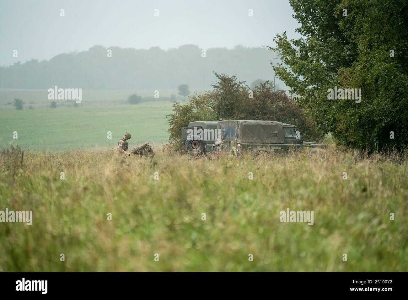 British army soldier prepares a field radio aerial mast, near two Land ...