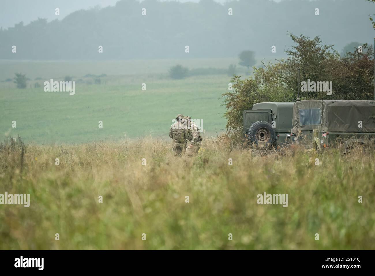 British army soldier prepares a field radio aerial mast, near two Land ...